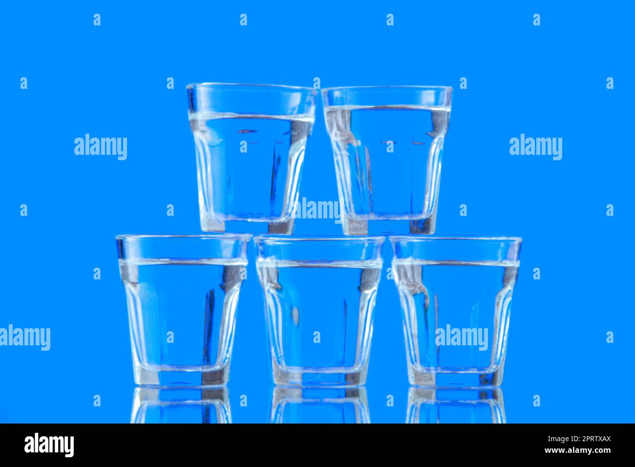 front view water glasses stacked on top of each other on blue isolated ...