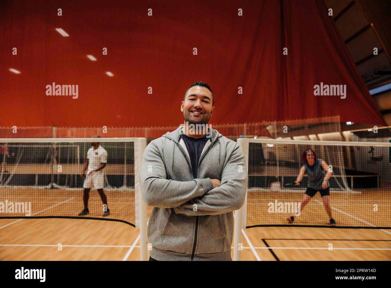 Smiling male coach standing with arms crossed at badminton court Stock ...
