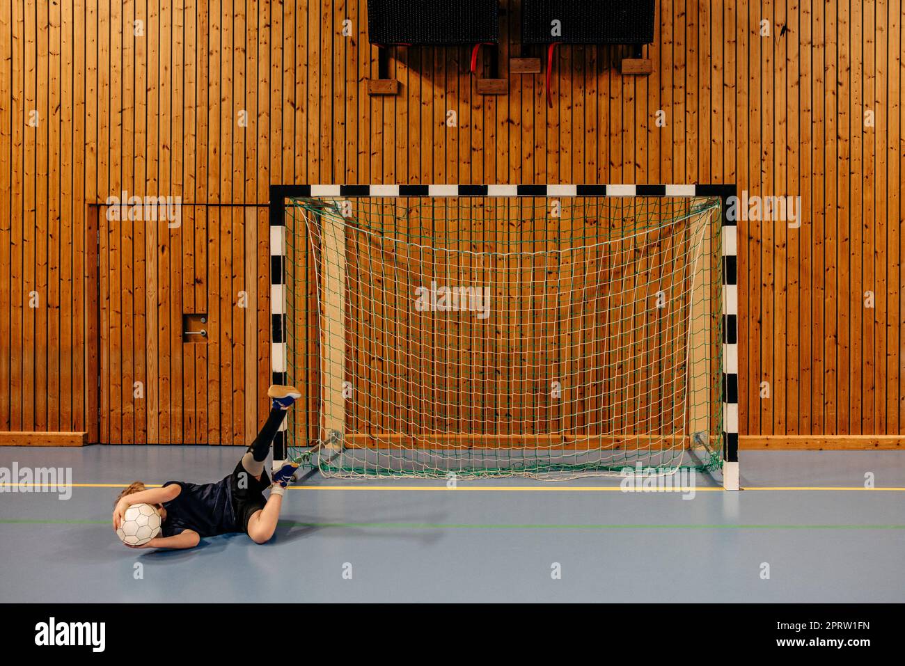 Male goalie with disabled leg lying on floor holding football while ...