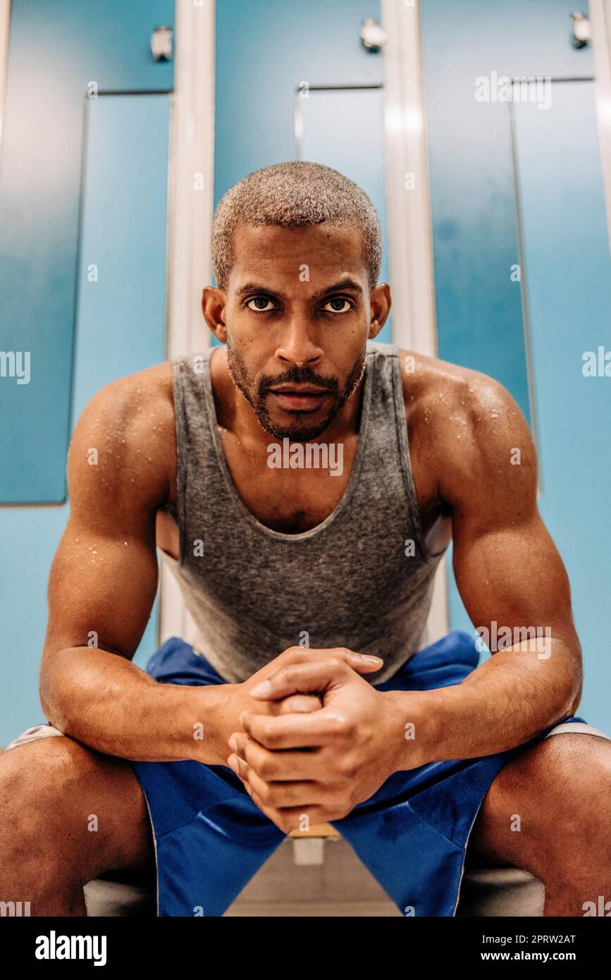 Determined male athlete with muscular build sitting in locker room ...