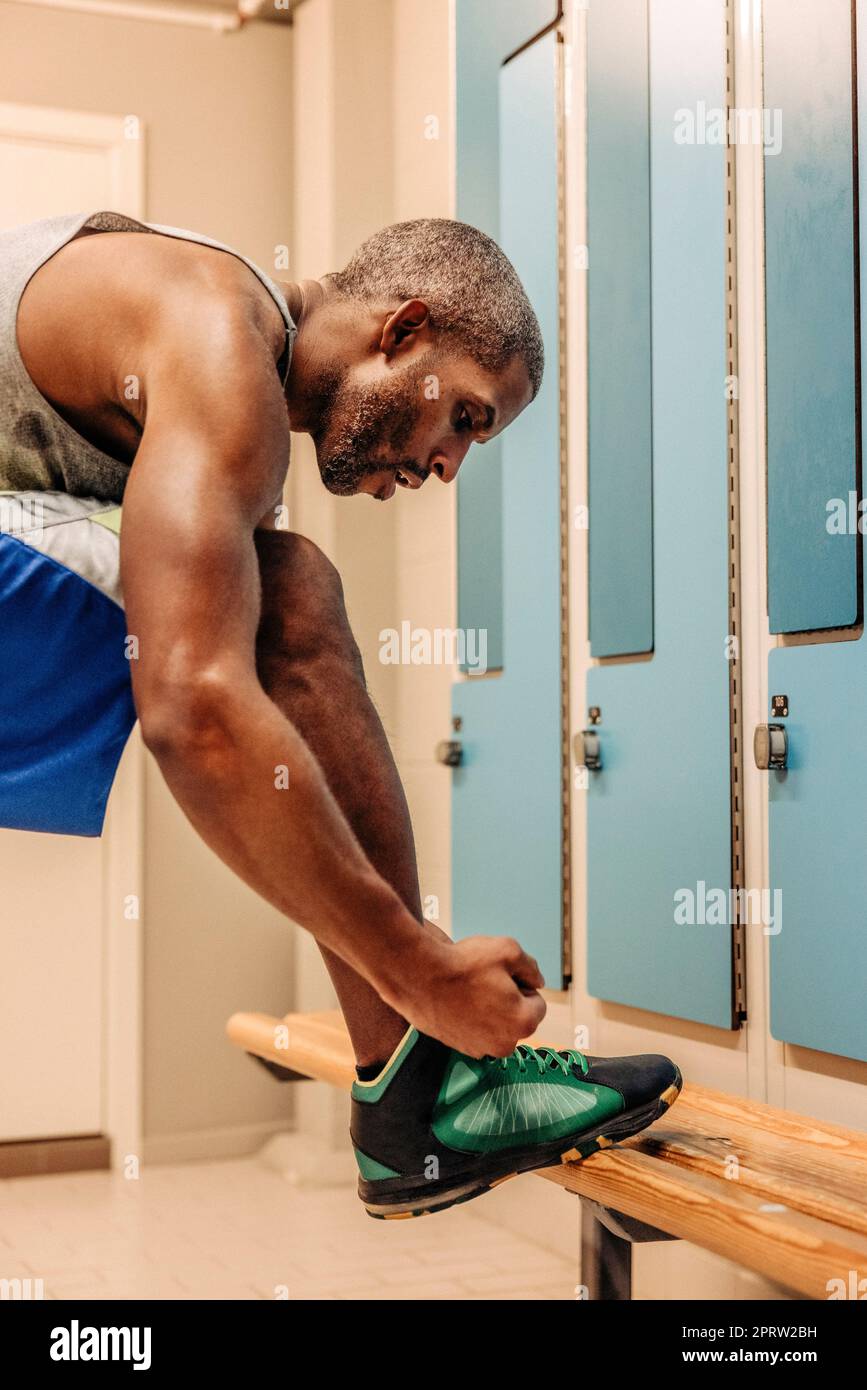 Male athlete tying shoe lace by bench in locker room Stock Photo - Alamy