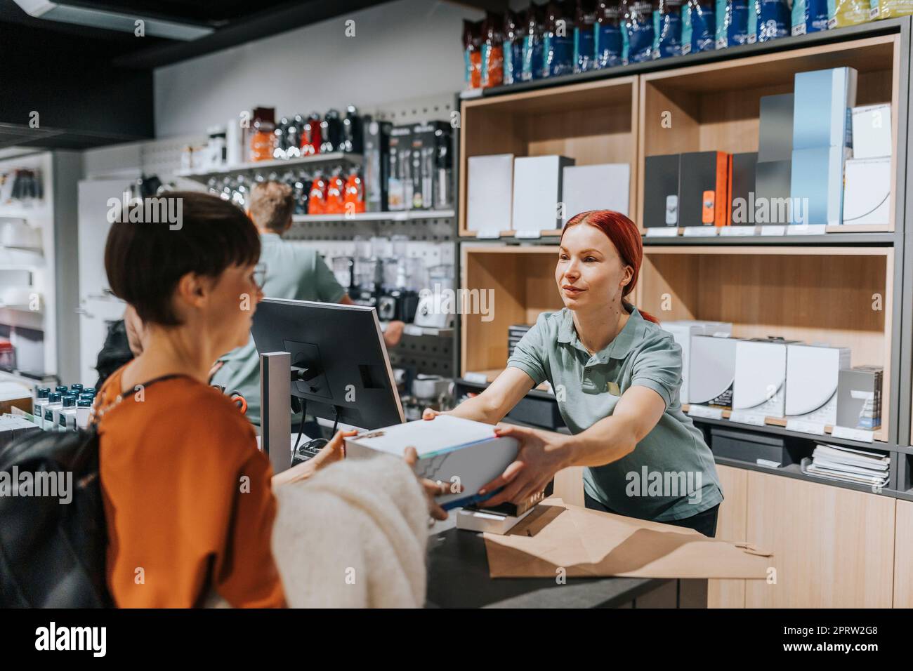 Female customer giving appliance box to sales clerk at checkout counter ...