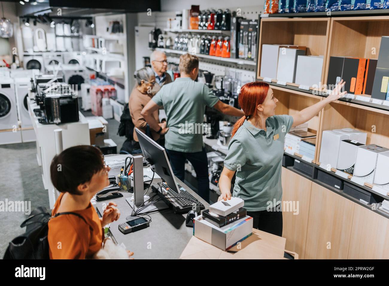 Female sales clerk showing various appliances on shelf to customer at ...