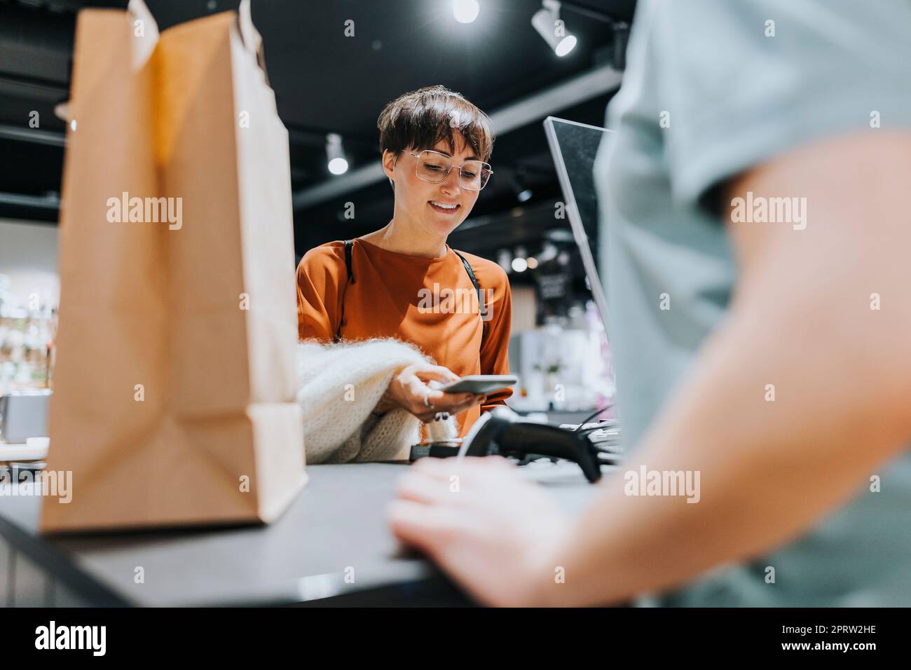 Smiling mature woman making payment through smart phone at checkout ...