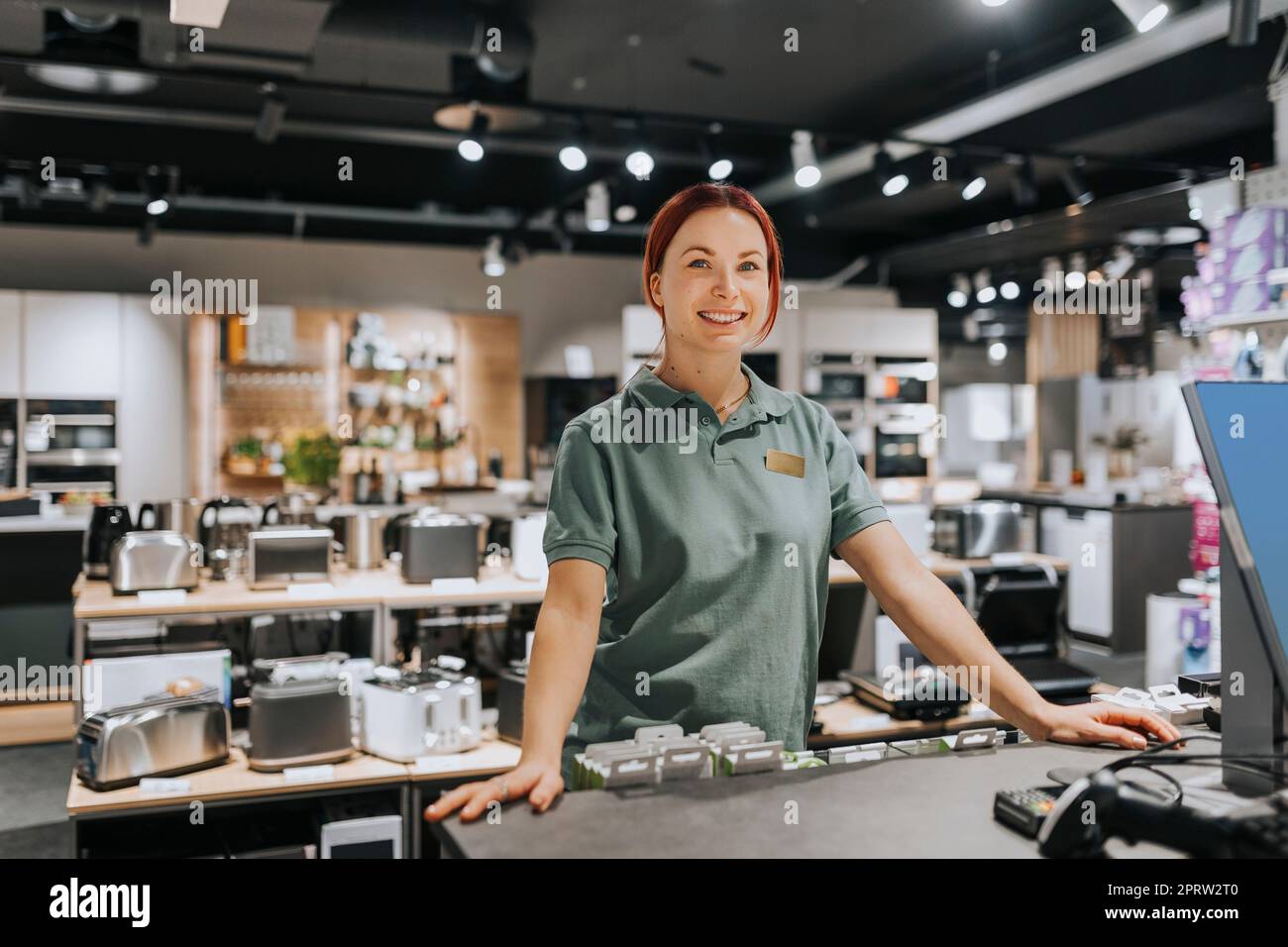 Portrait of smiling female sales clerk standing at counter in ...