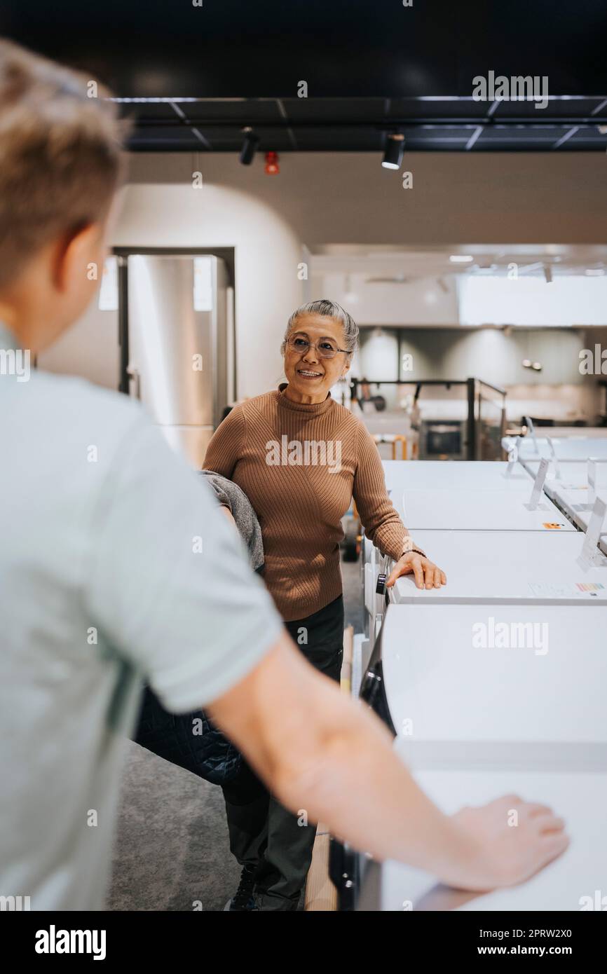 Senior woman discussing with male sales clerk by washing machines in ...