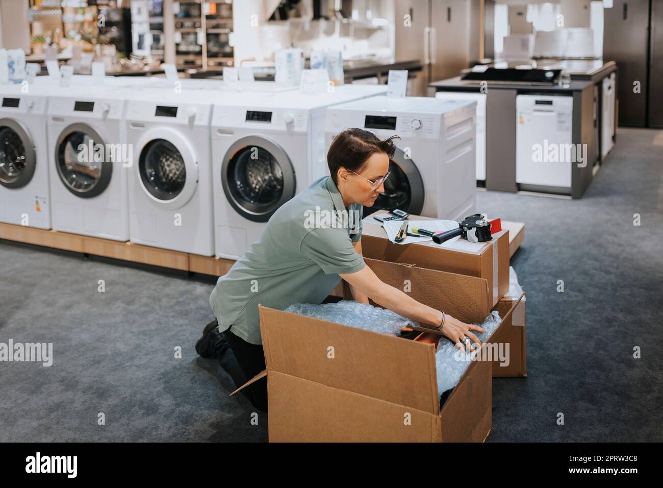Female retail clerk opening cardboard box while working in appliances ...