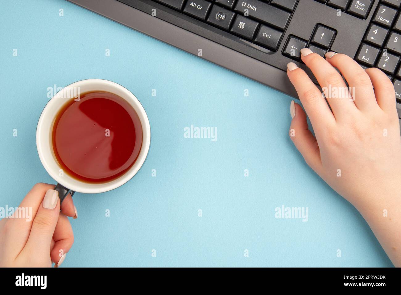 top view cup of tea in female hand keyboard on blue background Stock ...