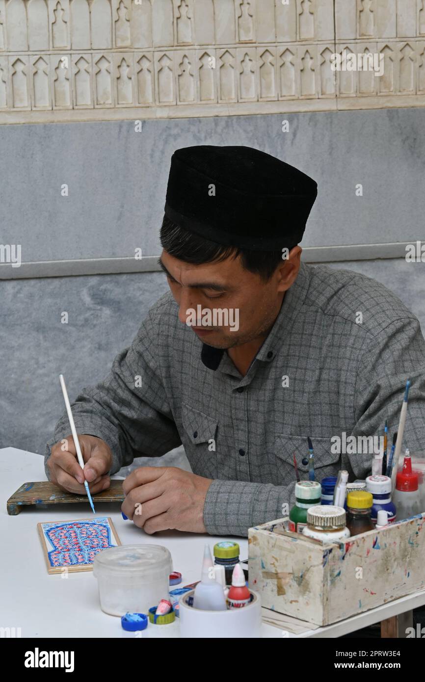 Uzbek man painting with a brush on a piece of ceramic in Bukhara ...