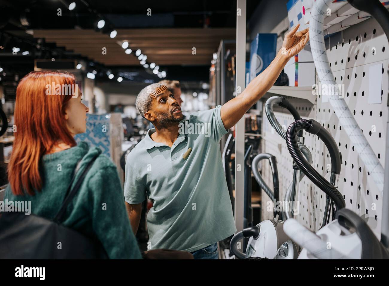 Salesman advising female customer in buying modern appliance at ...