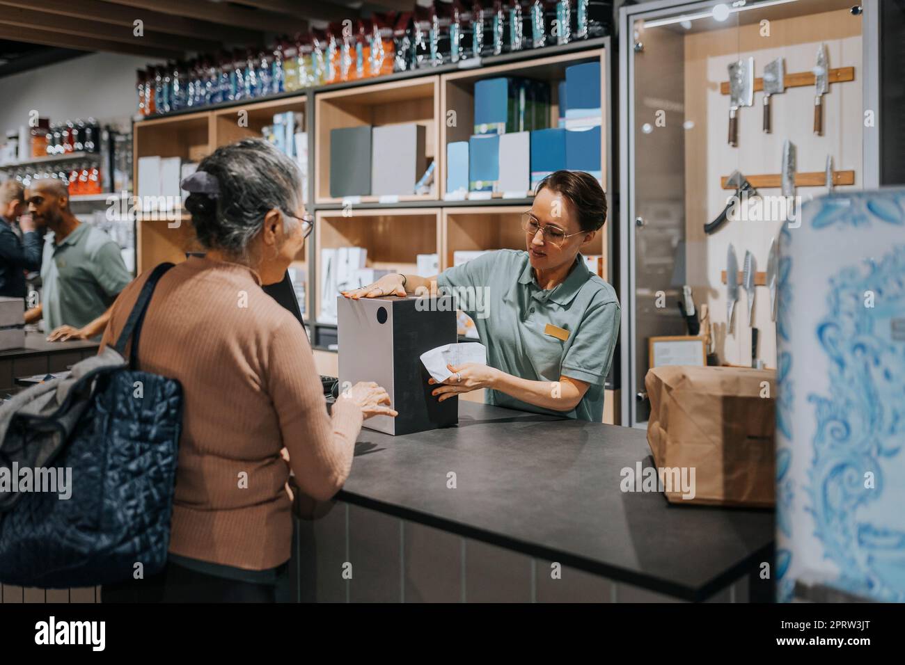 Female sales clerk giving appliance box to customer at checkout counter ...
