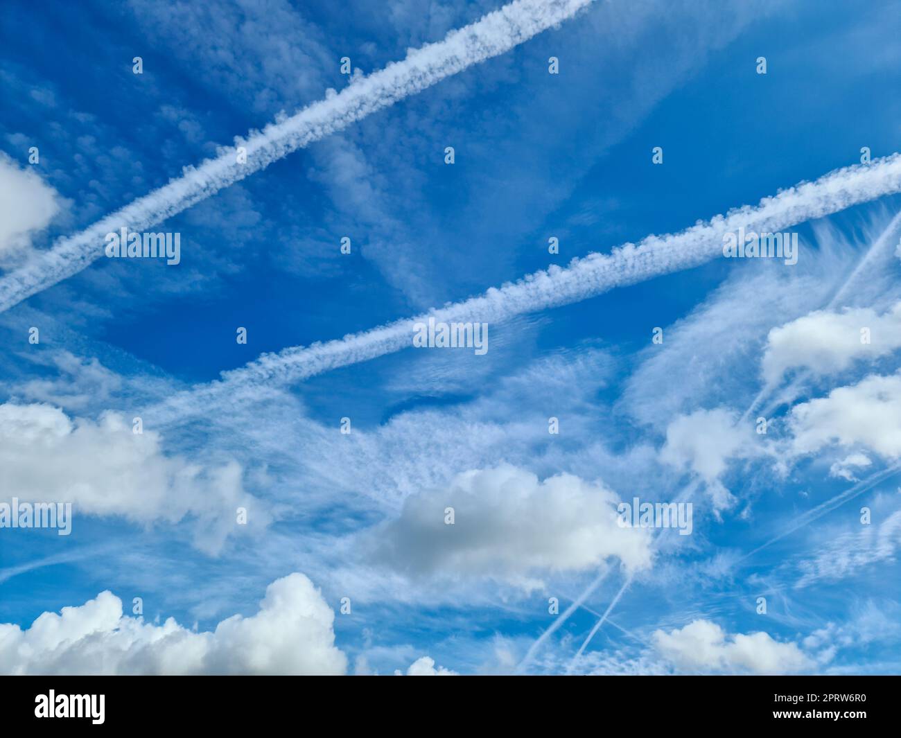 Aircraft condensation contrails in the blue sky inbetween some clouds ...