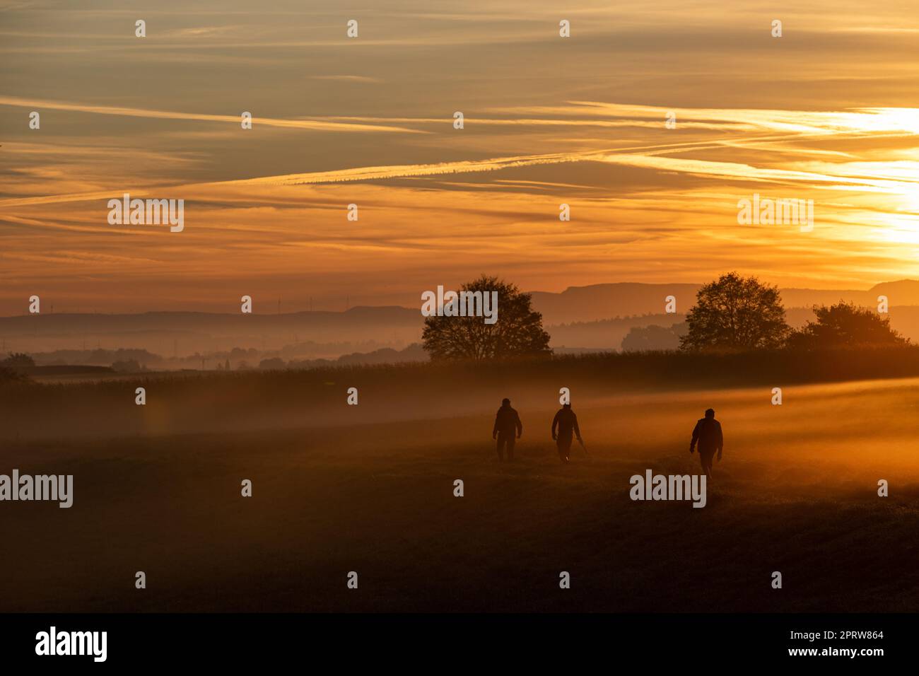 sunrise with three people walking through the mist in orange color ...