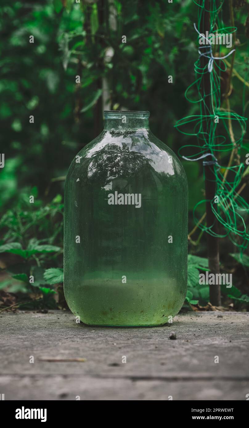 A glass transparent ten liter bottle of water stands in the garden ...