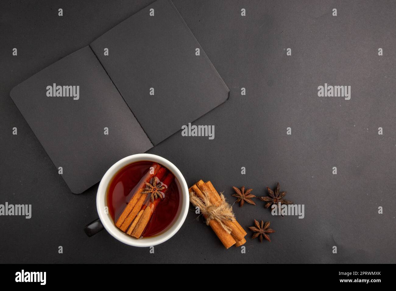 top view black notebook cup of tea flavored by cinnamon and anise ...