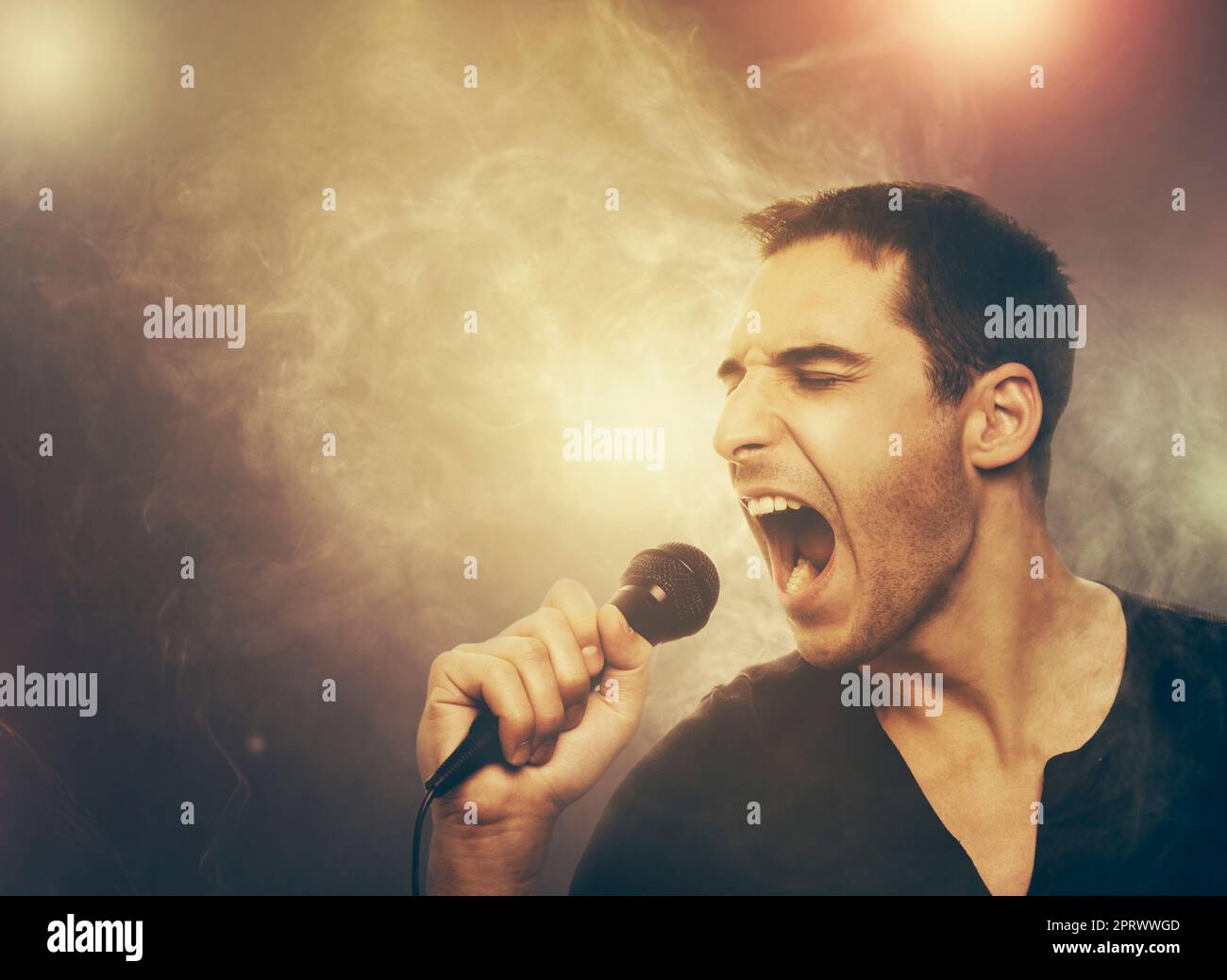 Young man singer holding microphone and singing karaoke music in night ...