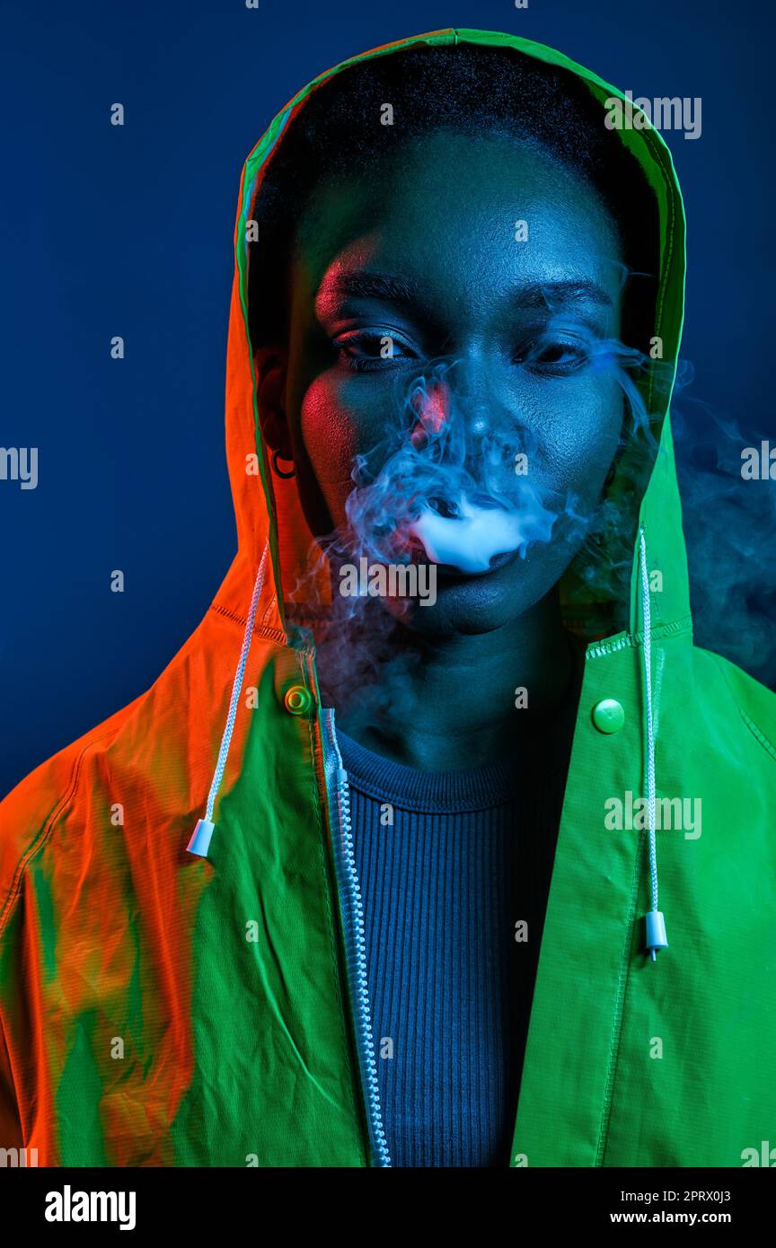 Hipster woman in raincoat blowing smoke from mouth Stock Photo - Alamy
