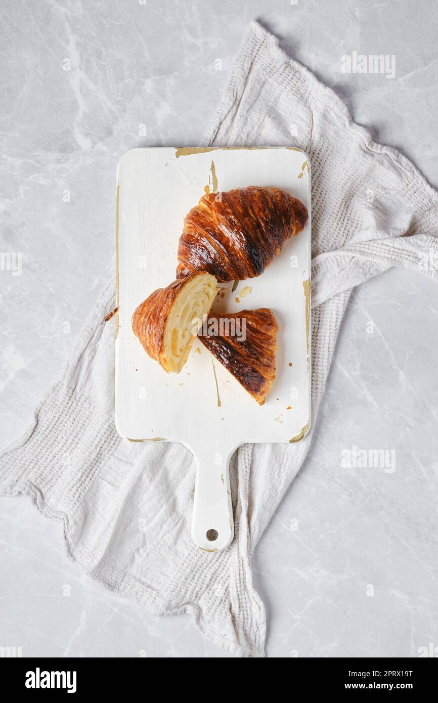 Overhead view of classic croissant cut on half on wooden serving board ...