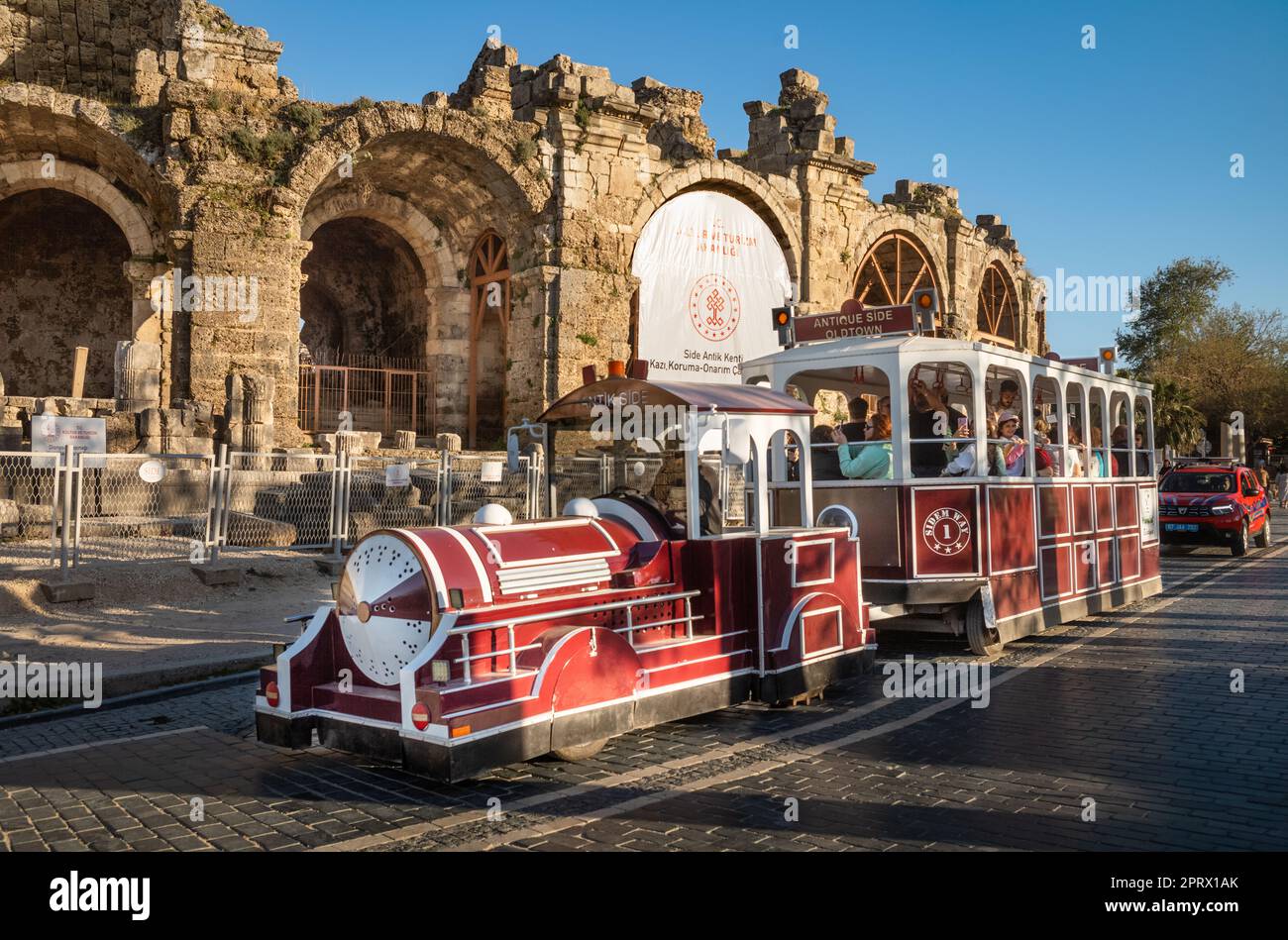 A fake train or tram carries tourists past the ruins of the ...