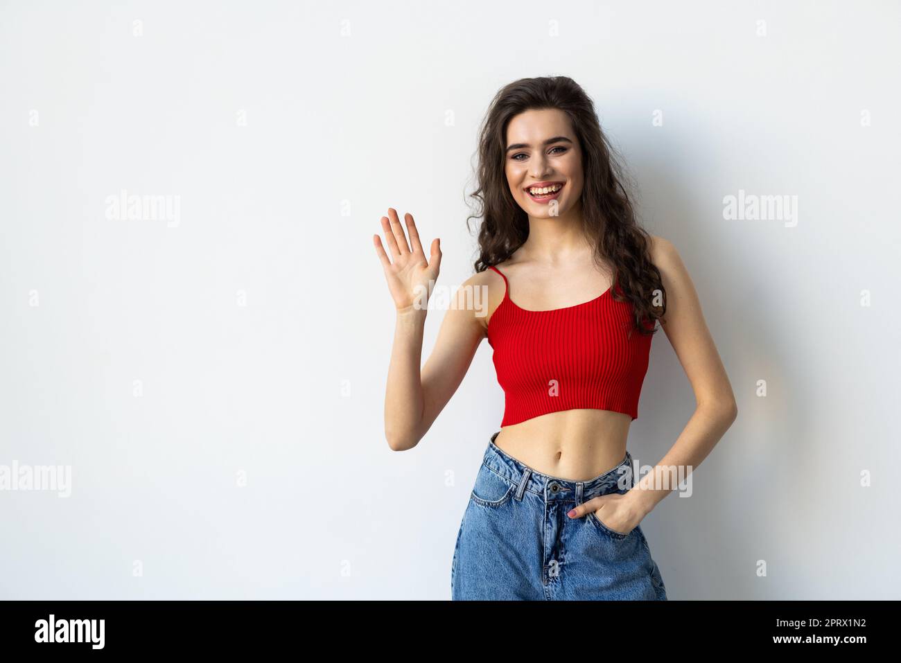 Friendly young woman say hi and wave hand cheerful, smiling at camera ...