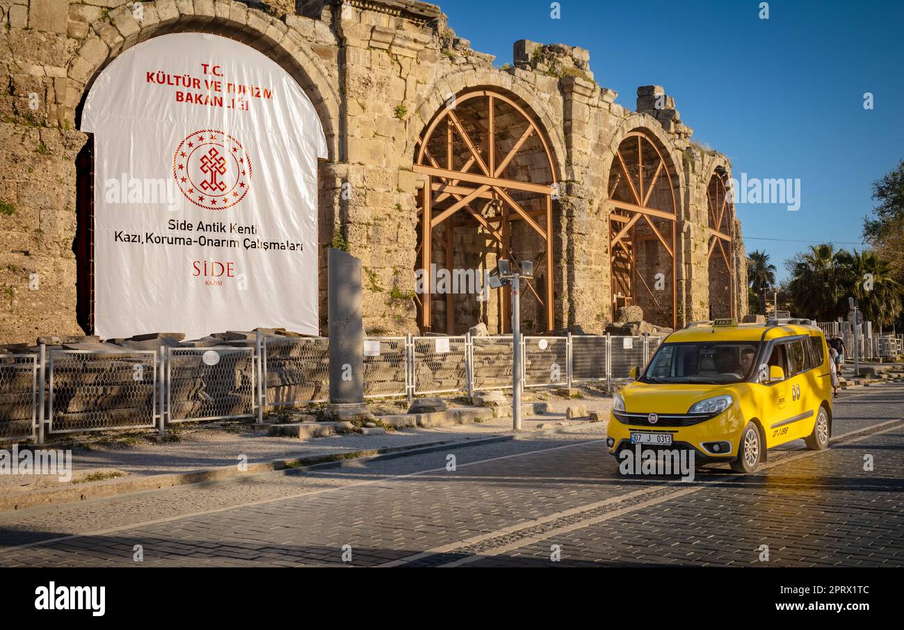 A yellow taxi passes the ruins of the amphitheatre in the ancient Roman ...