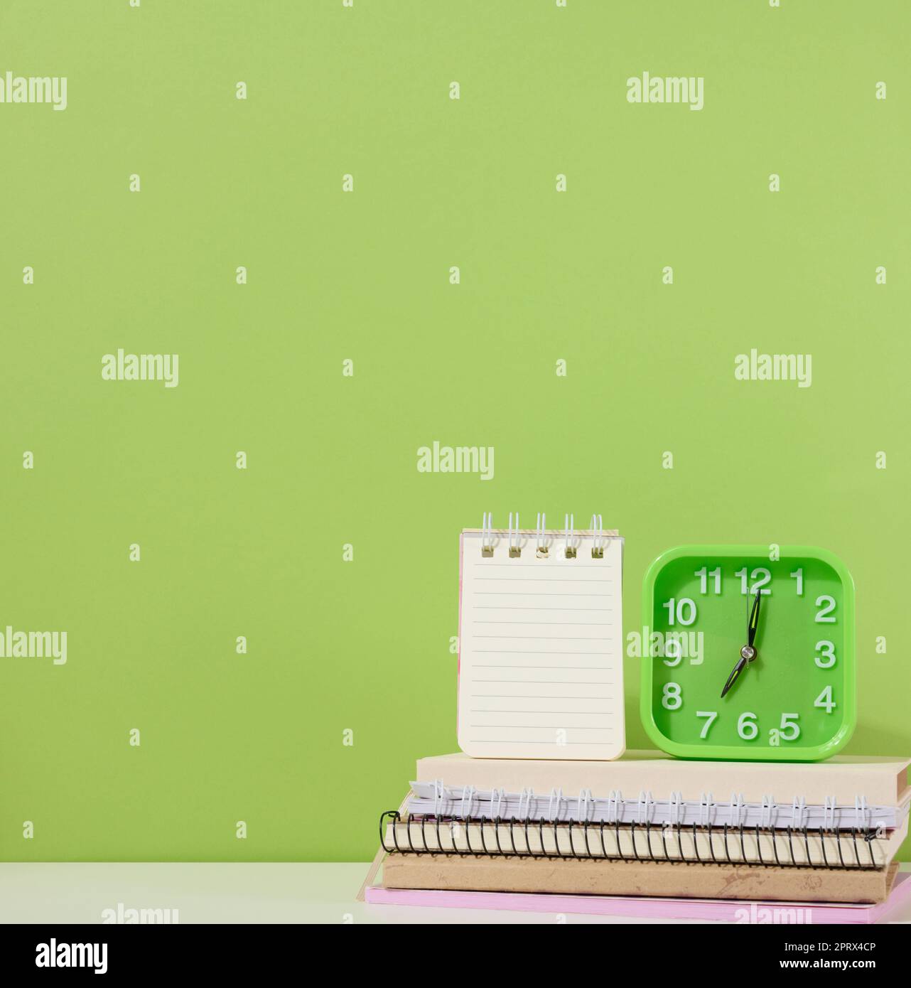 An open notepad and a green alarm clock stands on a stack of notebooks ...