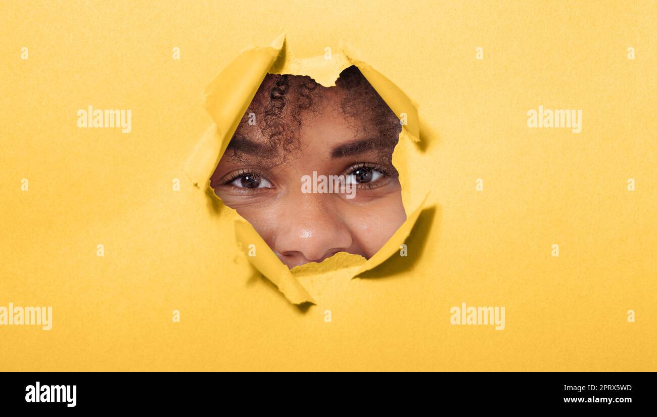 Surprised young African American woman looking playfully in torn paper ...