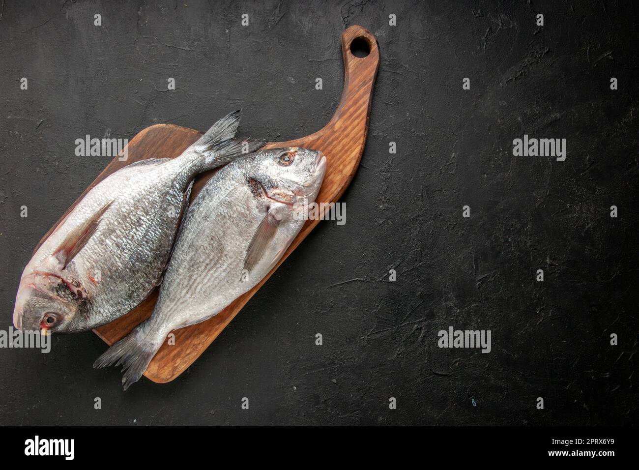 top view raw sea fish on chopping board on black table with free space ...
