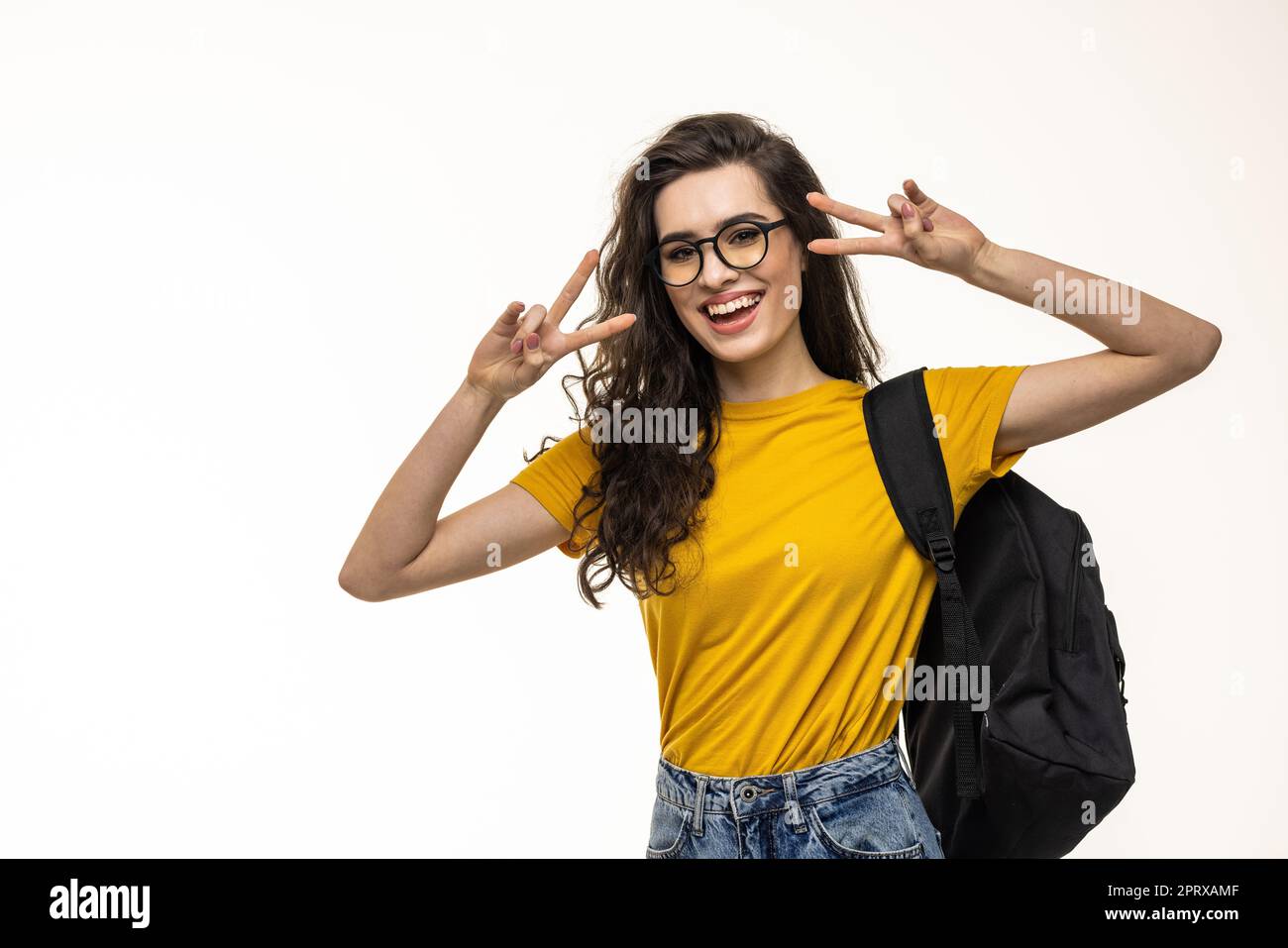 Lovely charismatic caucasian redhead girl with backpack, headphones over neck, showing peace ...