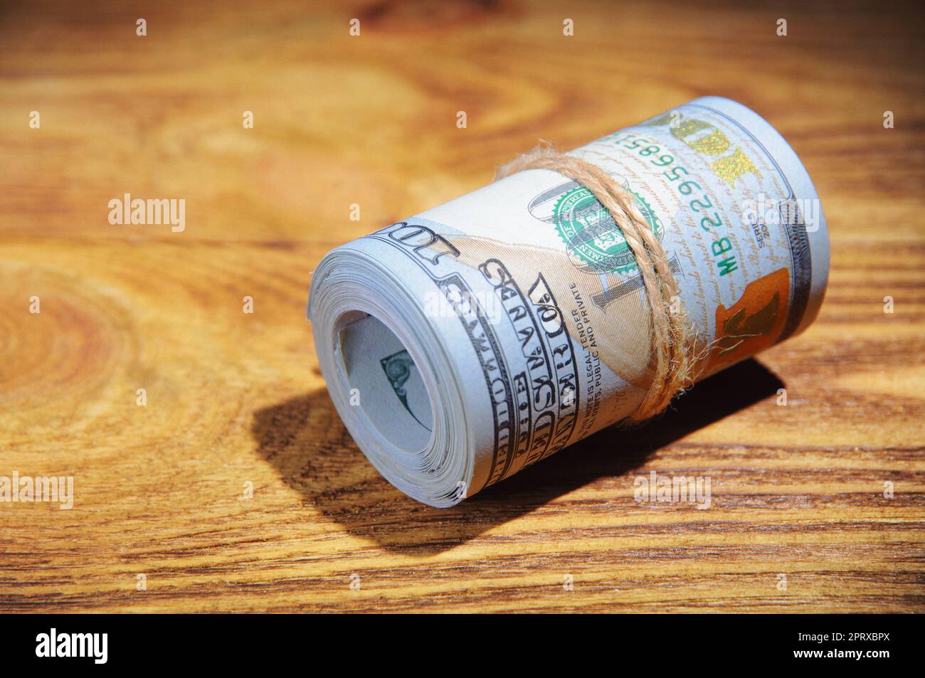 A roll of dollars on a wooden textured table in the dark illuminated by ...