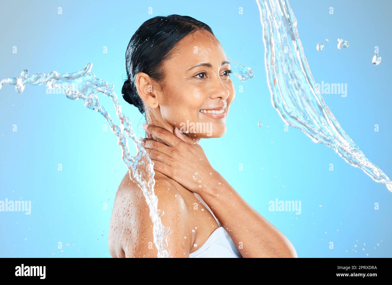 Mature woman, wet or water splash on blue background in studio skincare wellness, hygiene ...