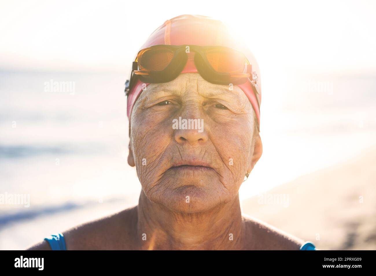 Senior woman at the beach, standing by the sea. Wearing a swimming cap ...