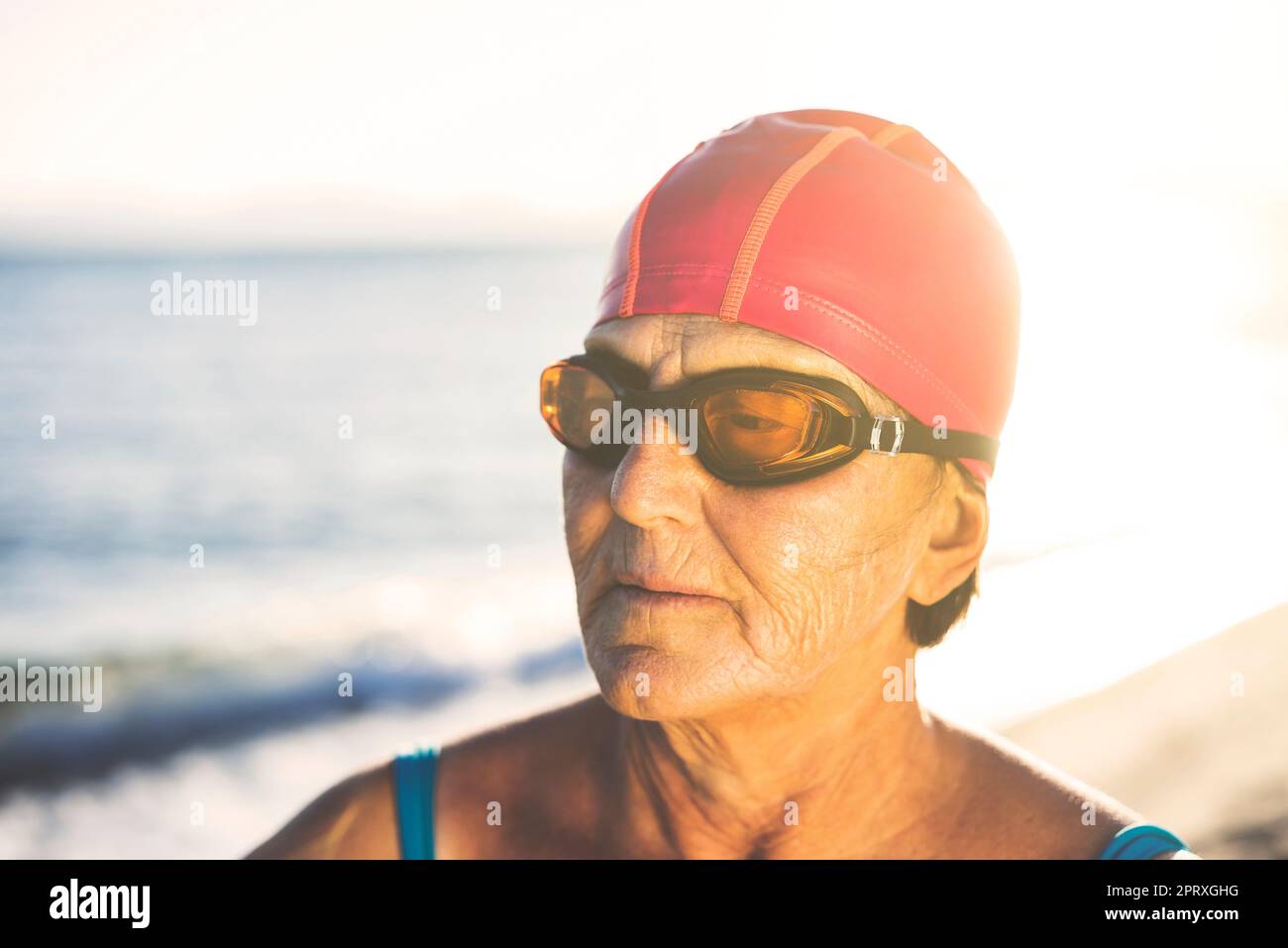 Senior woman at the beach, standing by the sea. Wearing a blue swimsuit ...
