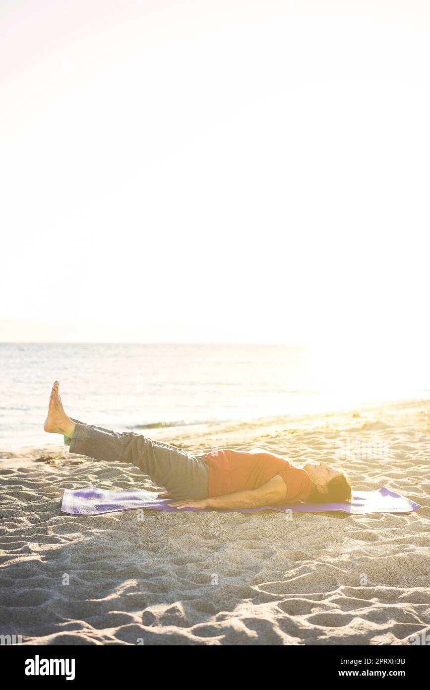 Senior woman at the beach laying on yoga mat, exercising. Doing double ...