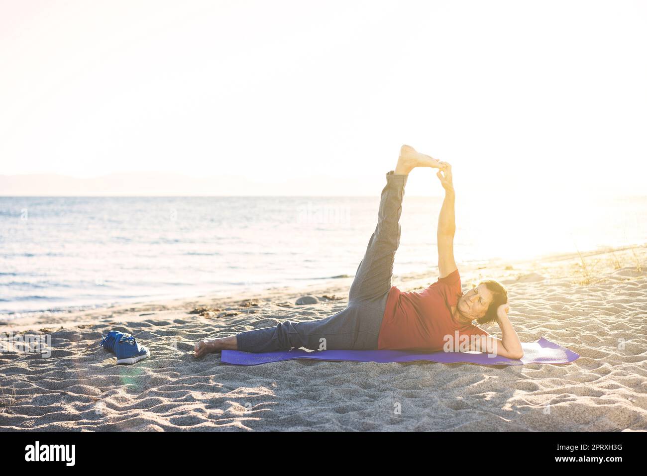 Senior woman at the beach laying on yoga mat, exercising. Doing side ...