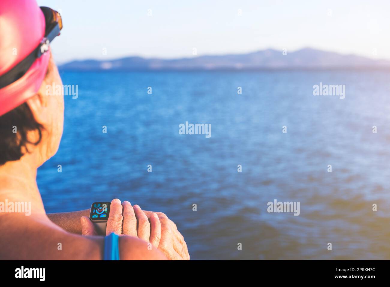 Back shot of senior woman at the beach, standing by the sea. Wearing a ...