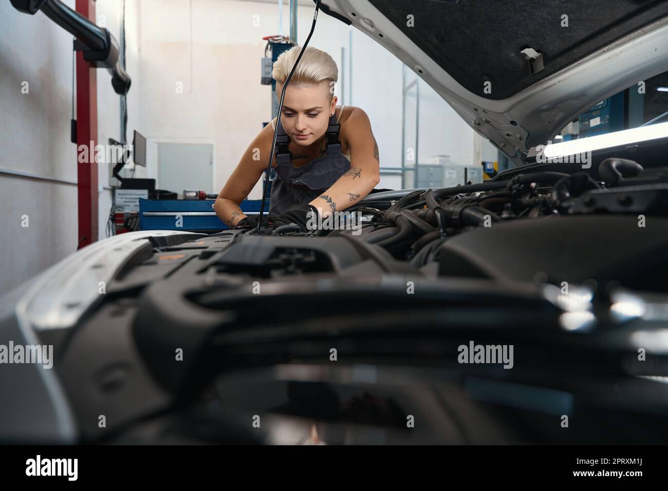 Pretty woman in work overalls works under hood of car Stock Photo - Alamy