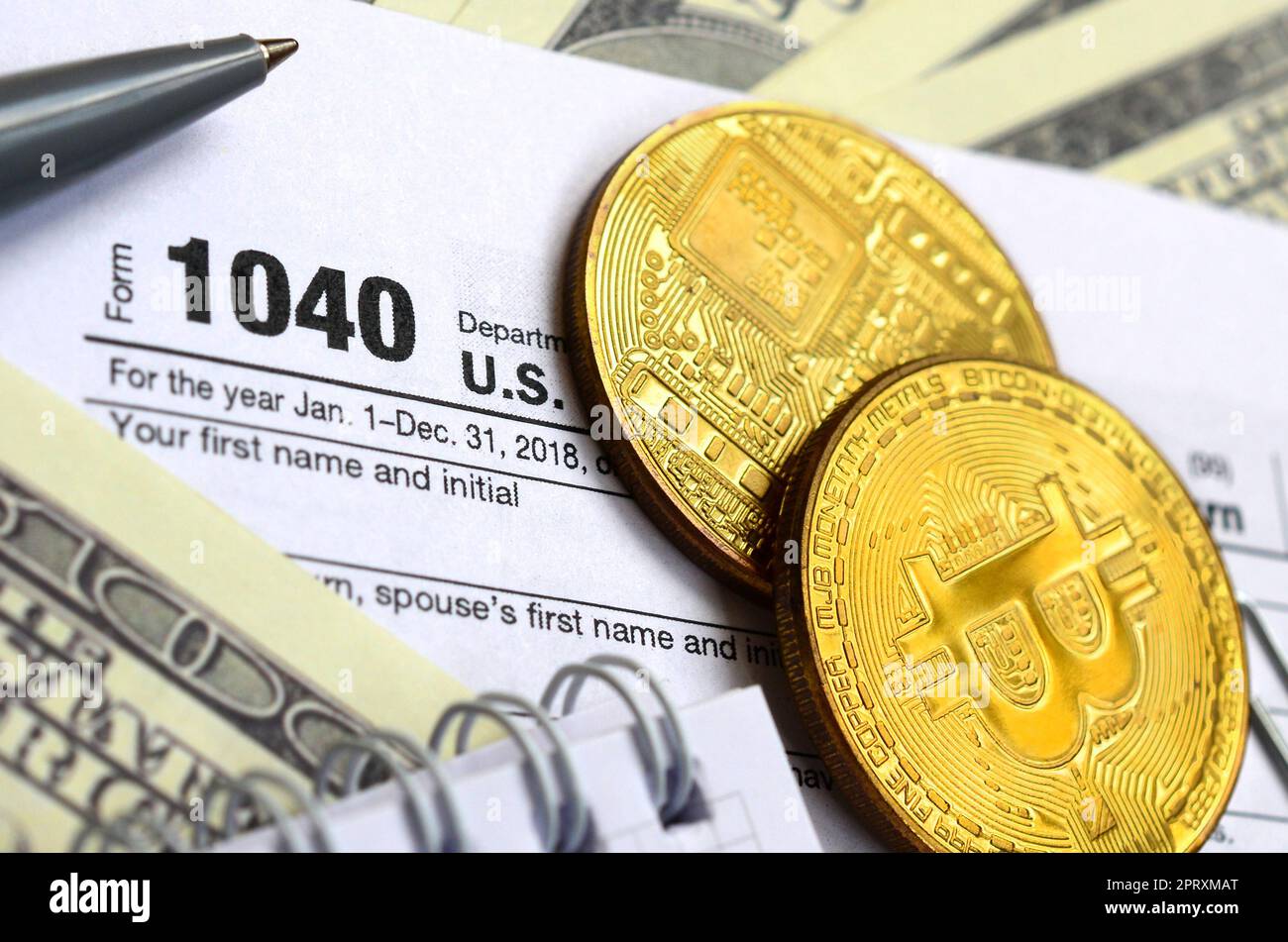 The pen, bitcoins and dollar bills is lies on the tax form 1040 U.S ...