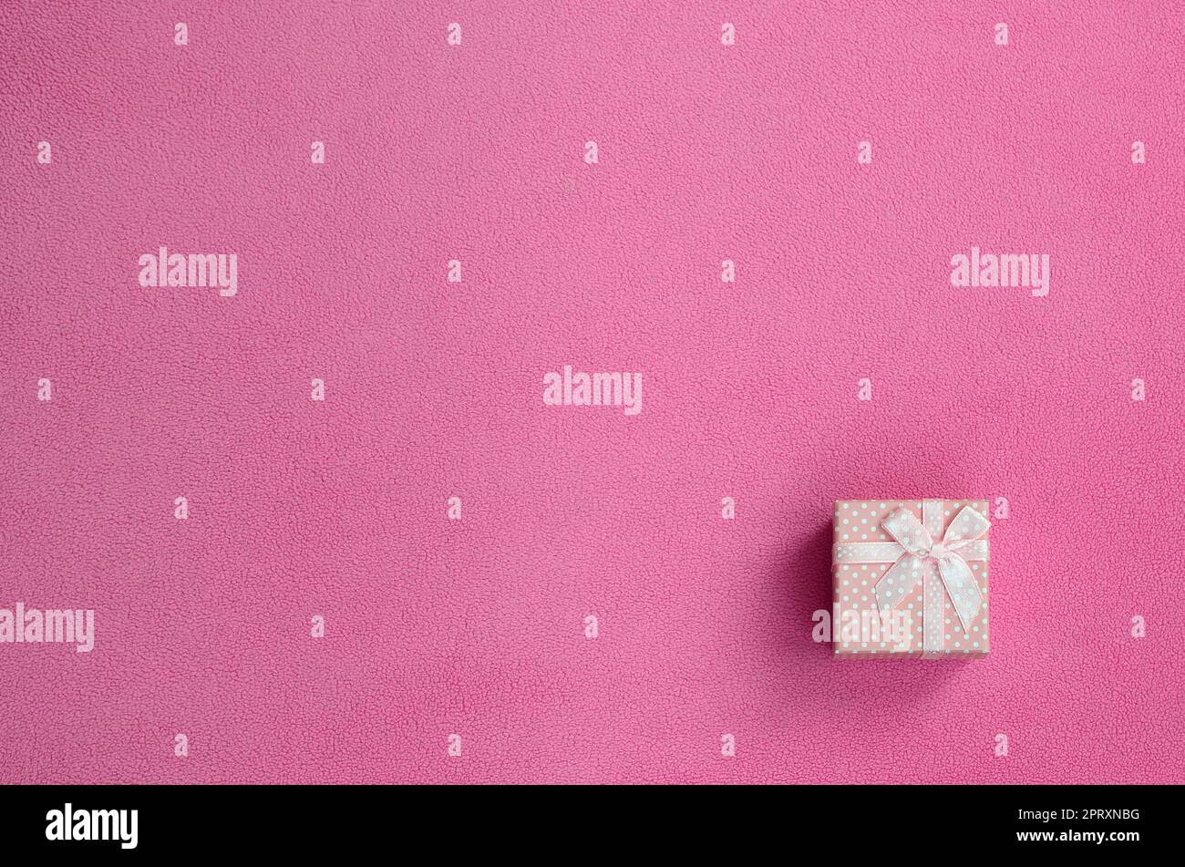 A small gift box in pink with a small bow lies on a blanket of soft and ...