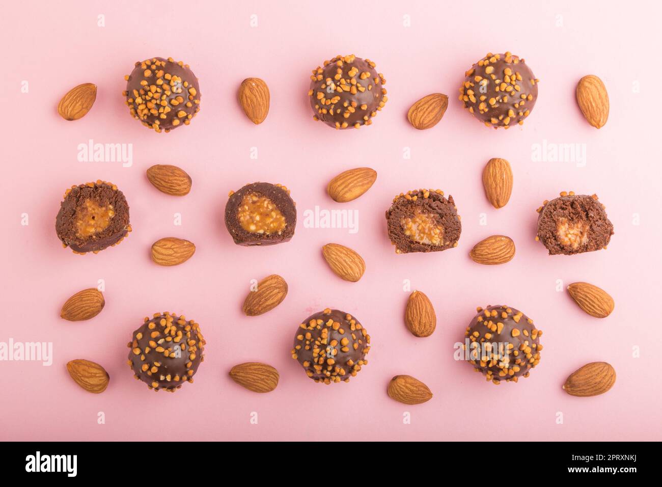 Chocolate caramel ball candies with almonds in a row on a pastel pink ...