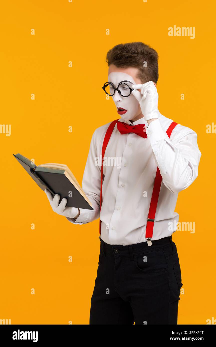 portrait of mime man artist reading book isolated on yellow background ...