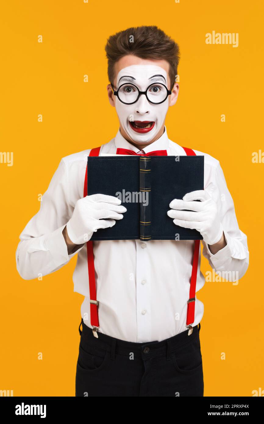 portrait of surprised mime man artist reading book isolated on yellow ...