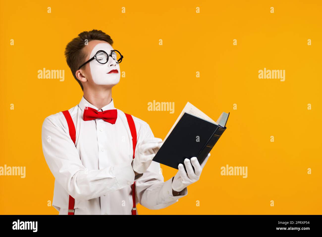 portrait of mime man artist reading book isolated on yellow background ...