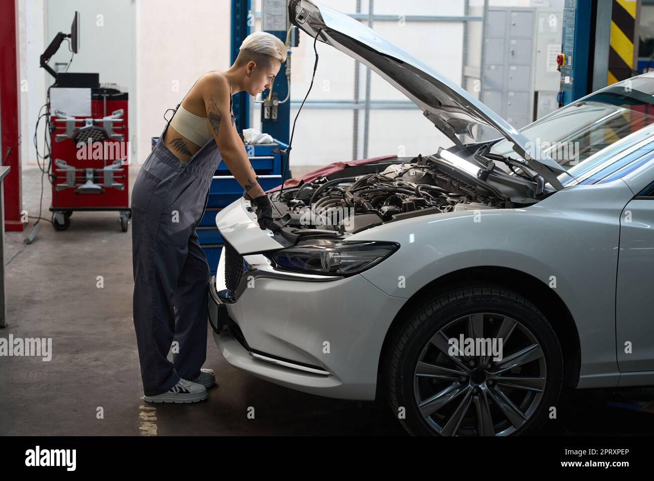 Pretty woman in a car repair shop inspects car engine Stock Photo - Alamy