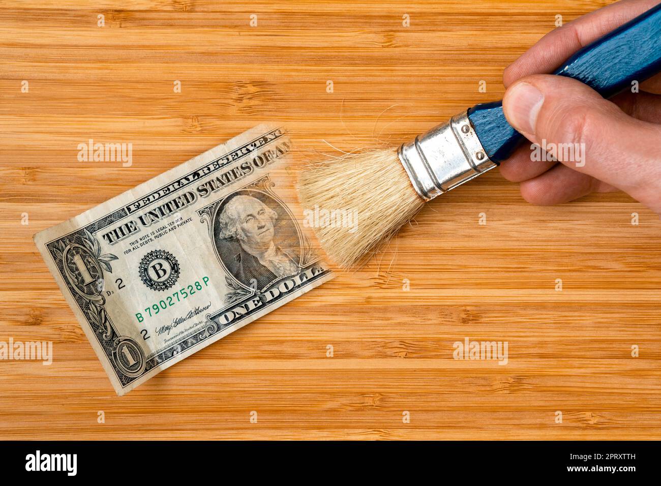 Hand with a brush painting one dollar bill on the wooden background ...