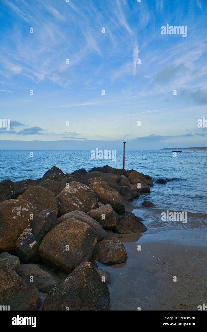 Stone groyne juts out into the water off the coast in Denmark. Sunny ...