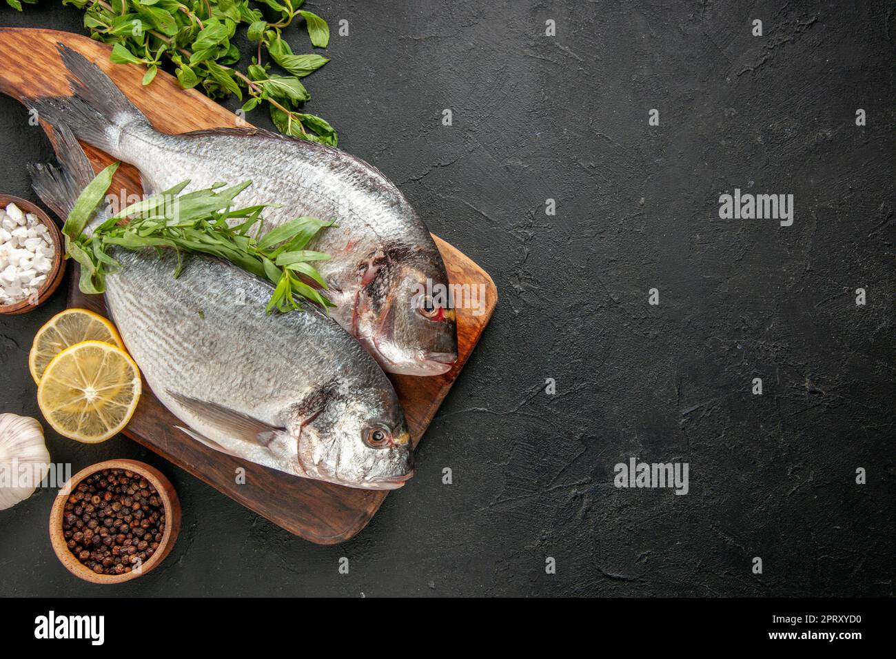 top view raw sea fish on chopping board sea salt black pepper in bowls ...