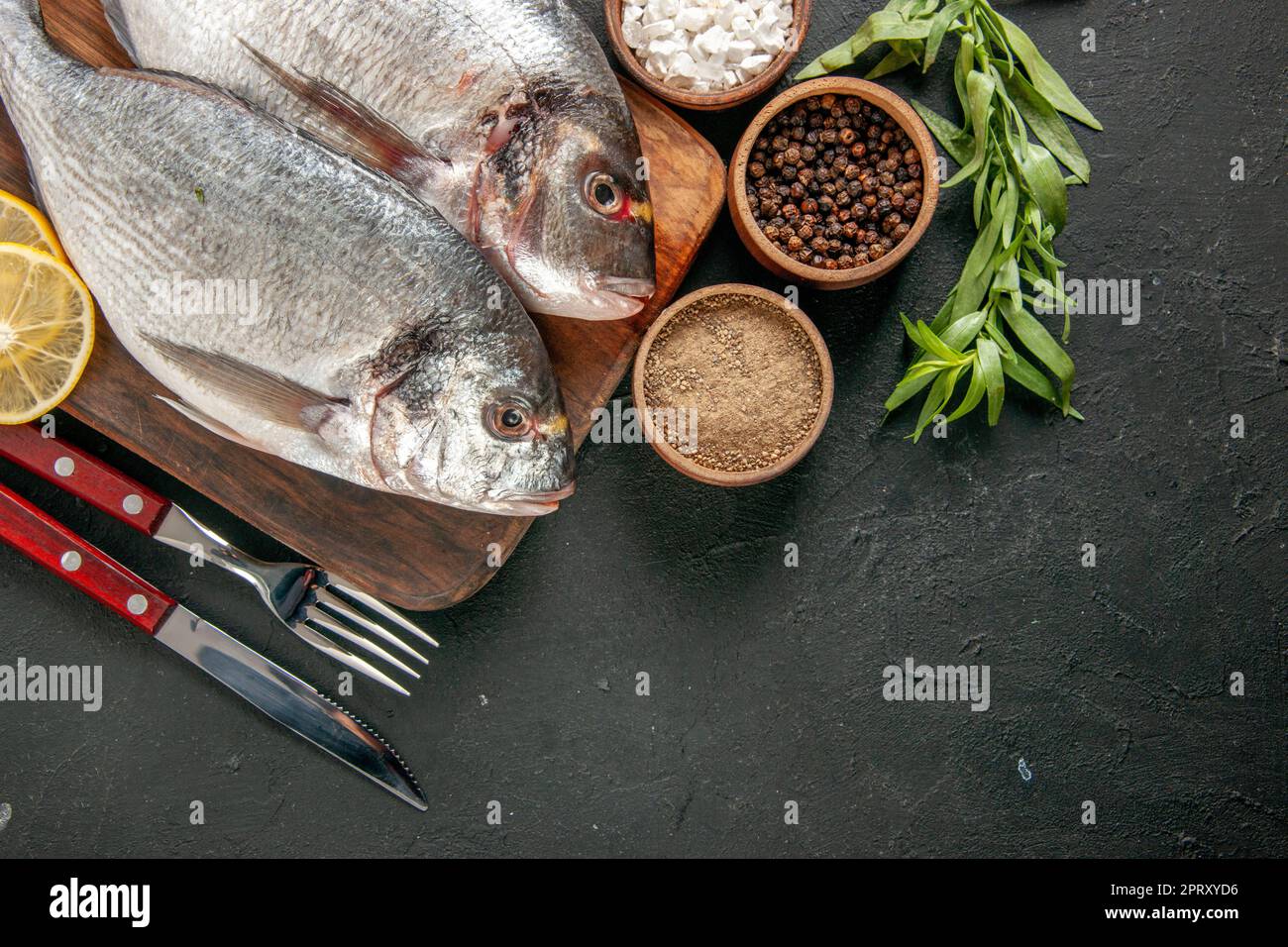 top view raw sea fish on chopping board sea salt black pepper in bowls ...