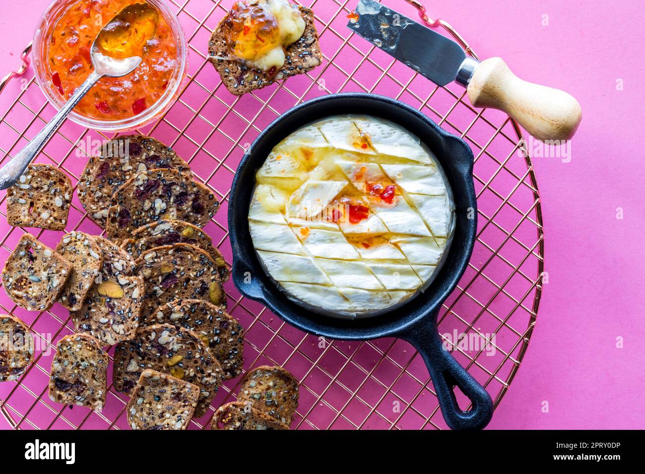 A baked brie in a cast iron fry pan served with crackers and red pepper ...