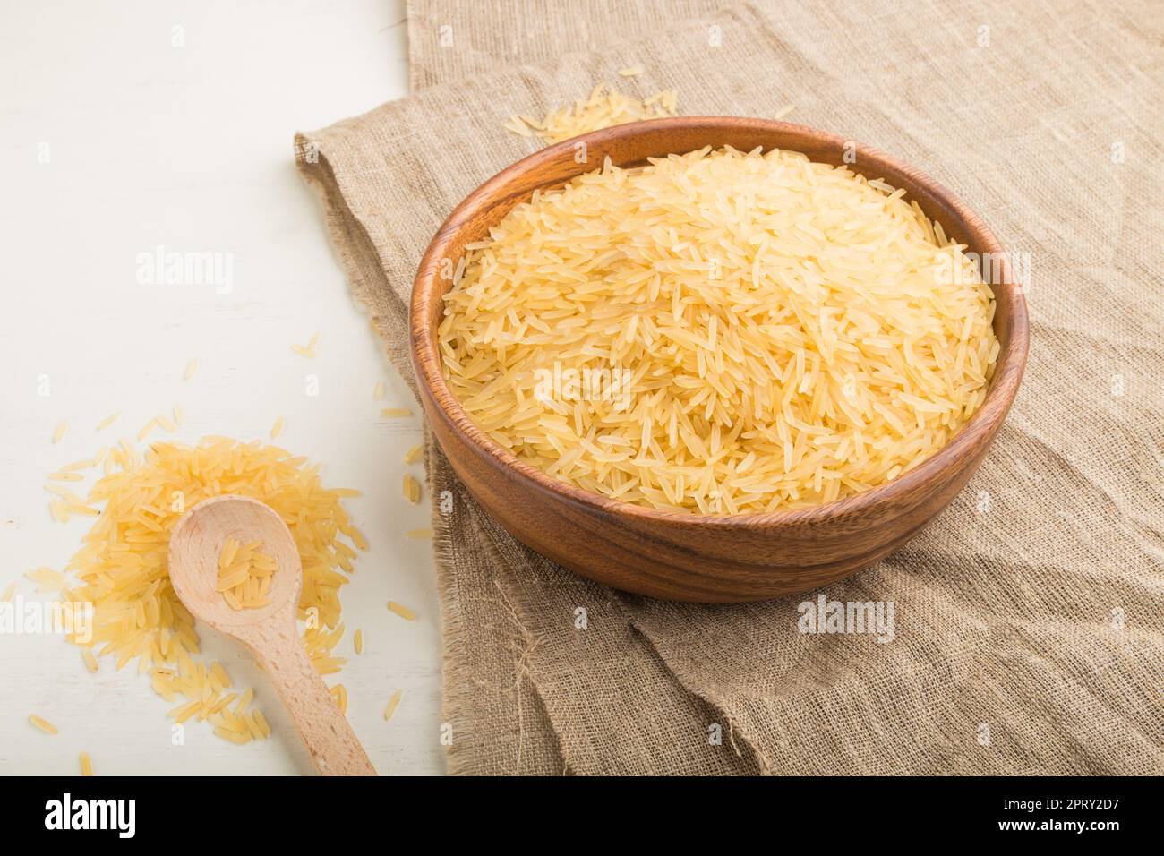 Wooden bowl with raw golden rice and wooden spoon on a white wooden ...